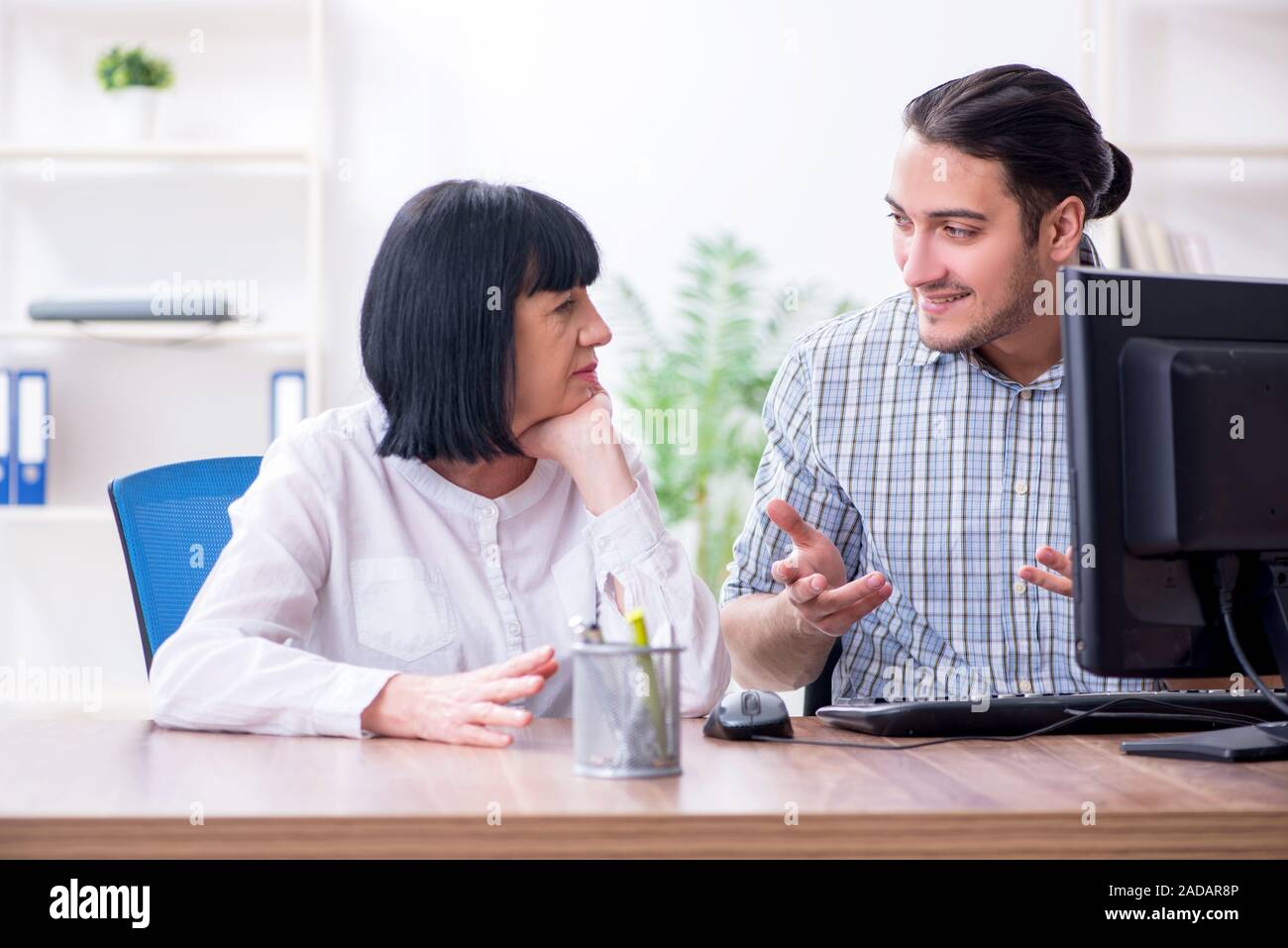 Young male employee explaining to old female colleague how to us Stock ...