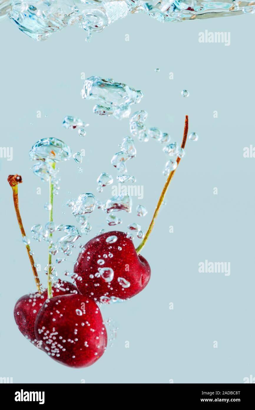 Close-up of two falling cherries followed by bubbles in front of bright ...