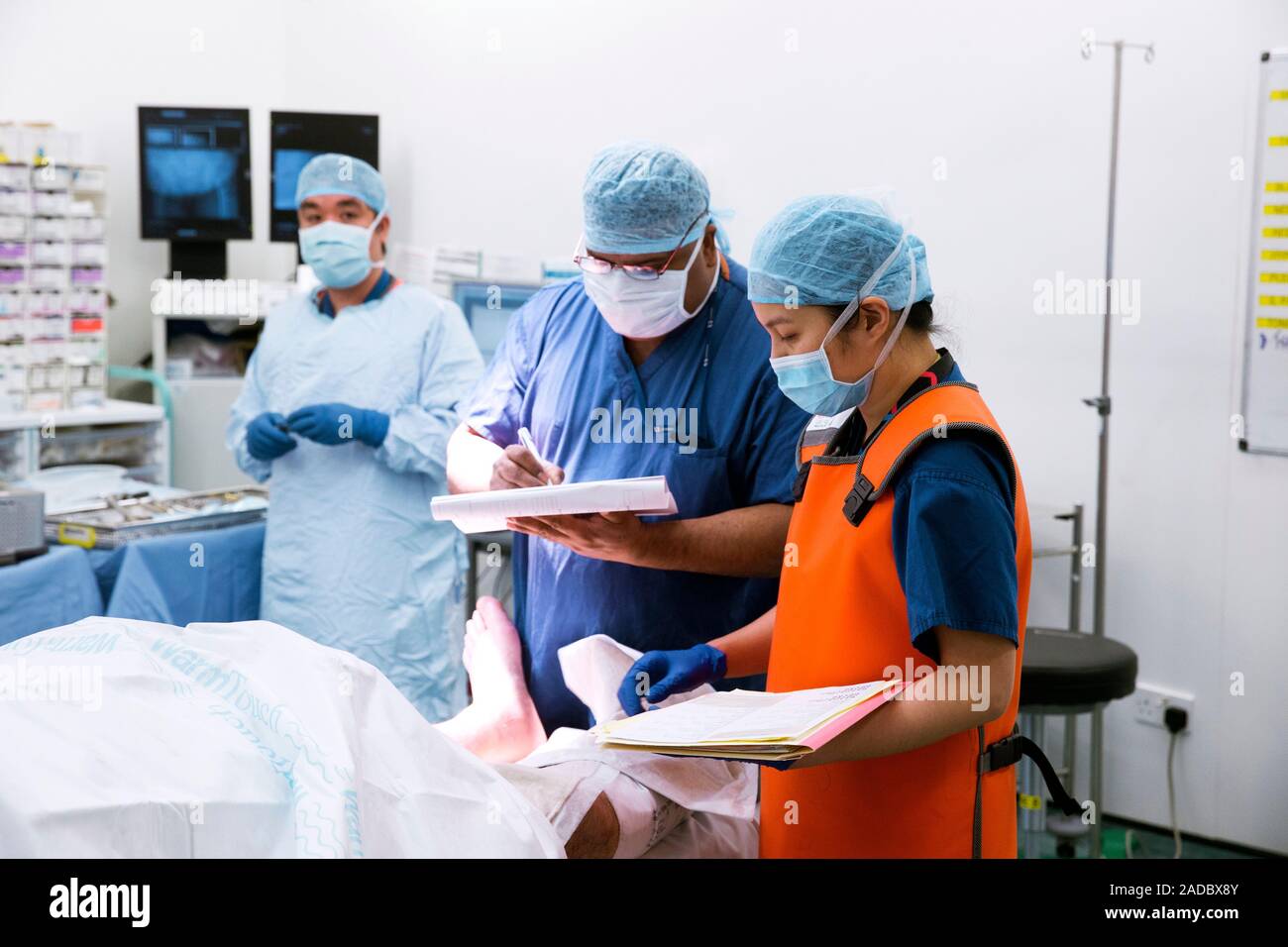 Hospital operation. Nurses checking a patient's notes during surgery in ...