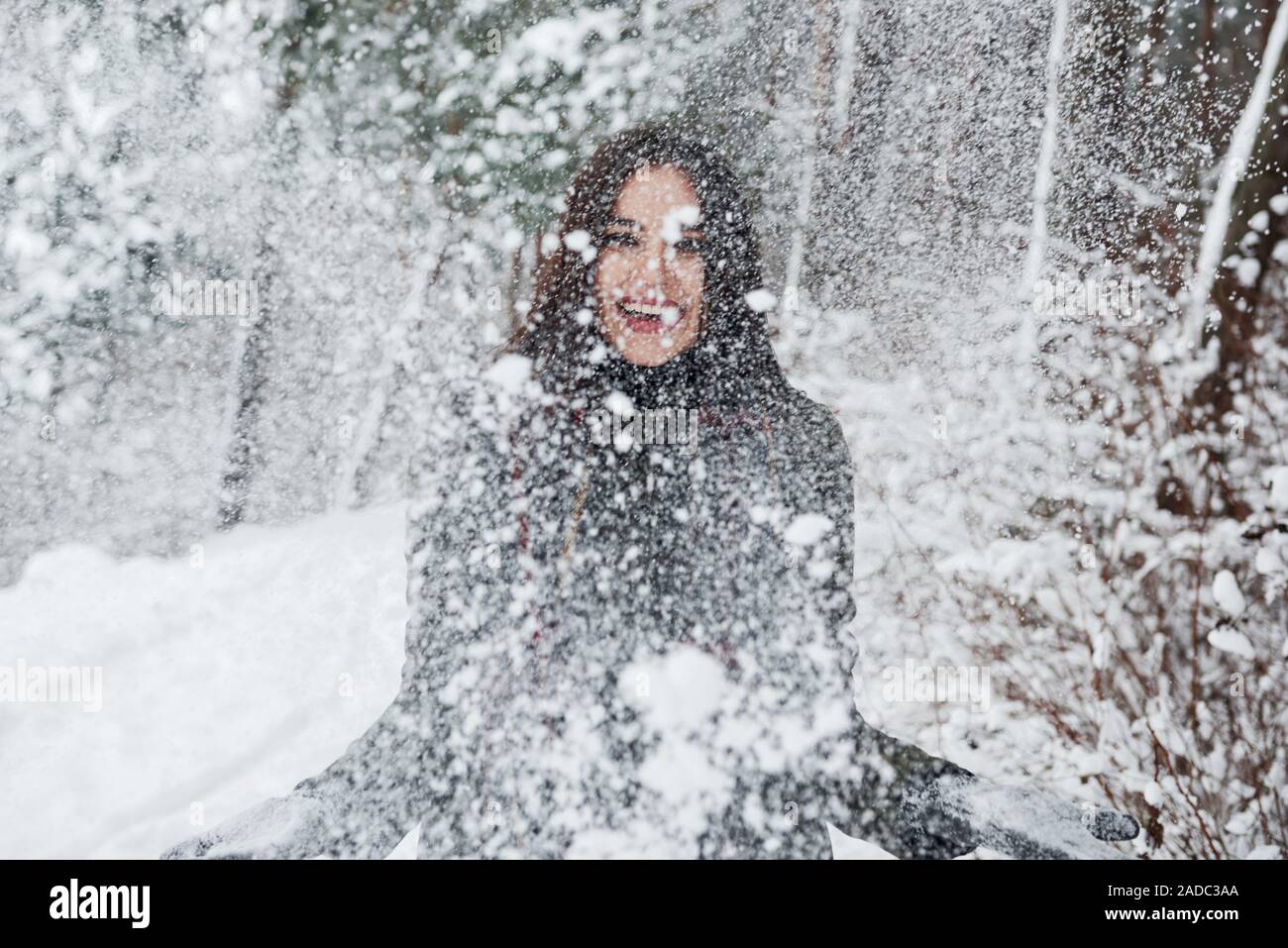 Playful young girl standing outdoors and throwing up the snow ...