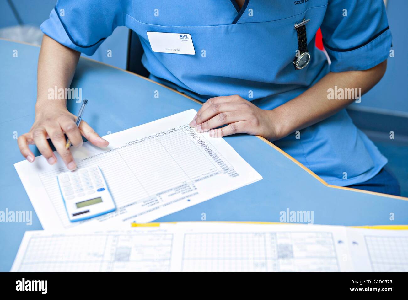 Nurse writing up notes. Close-up of a hospital nurse using a calculator ...