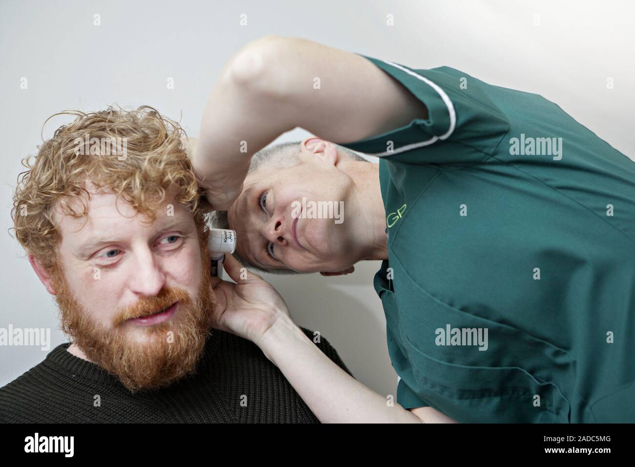 Ear examination. Paramedic at a general practice (GP) clinic using an ...
