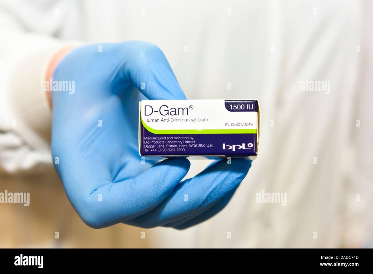 Anti-D immunoglobulin. Gloved hand holding the packaging for D-Gam, a ...