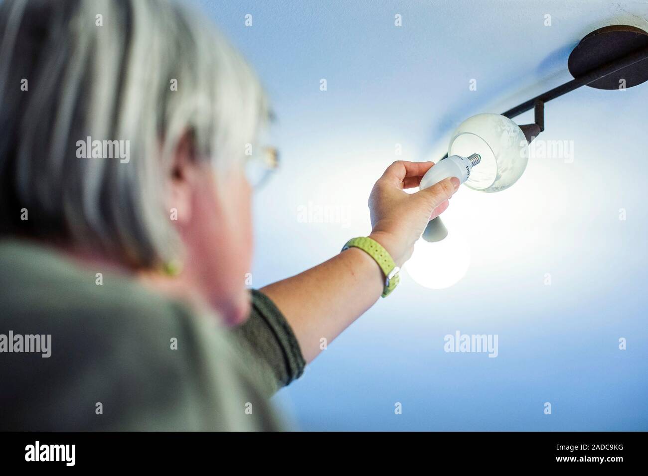 Changing a light bulb. Woman changing a light bulb for an overhead lamp ...
