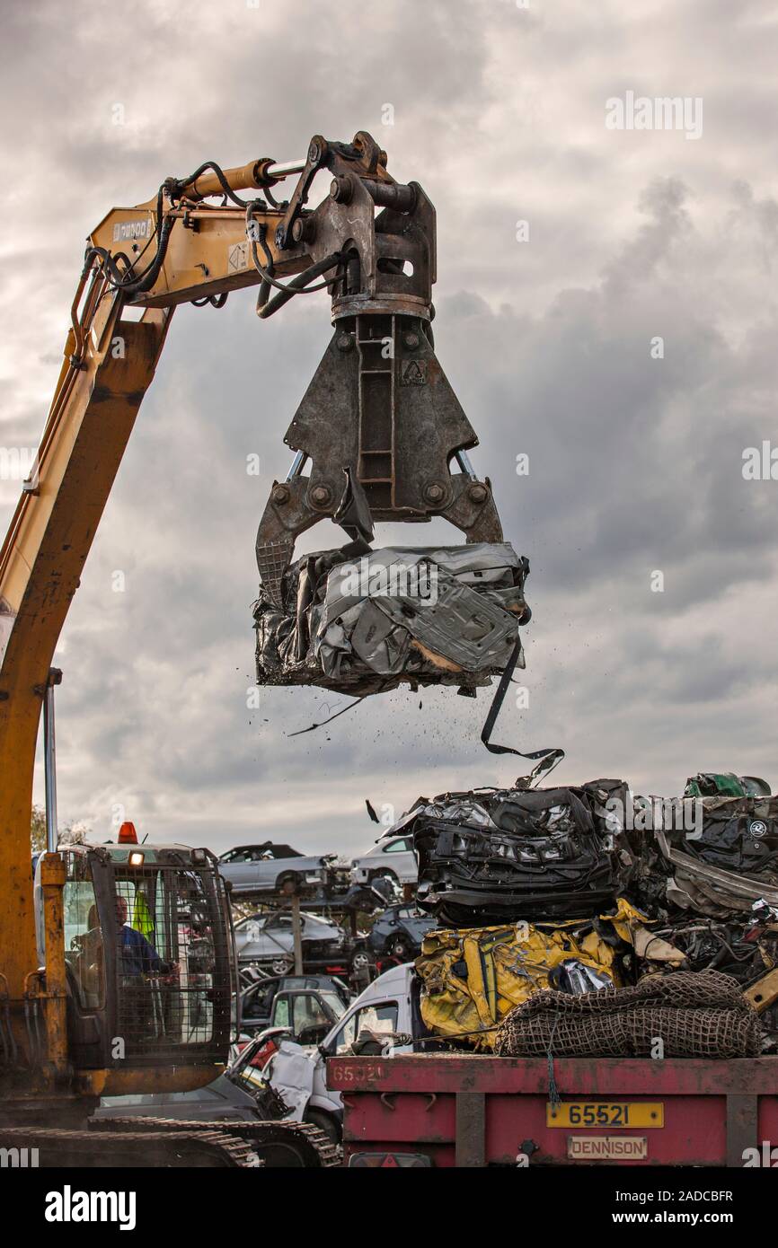 Scrapyard. Crushed cars being loaded onto a transporter at a scrapyard ...