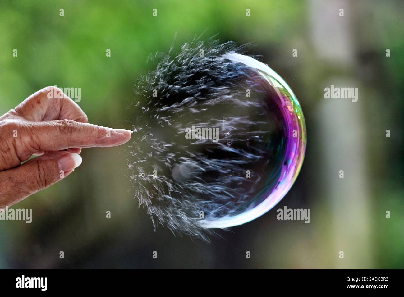 High-speed photograph of a hand popping a soap bubble in mid-air. The ...