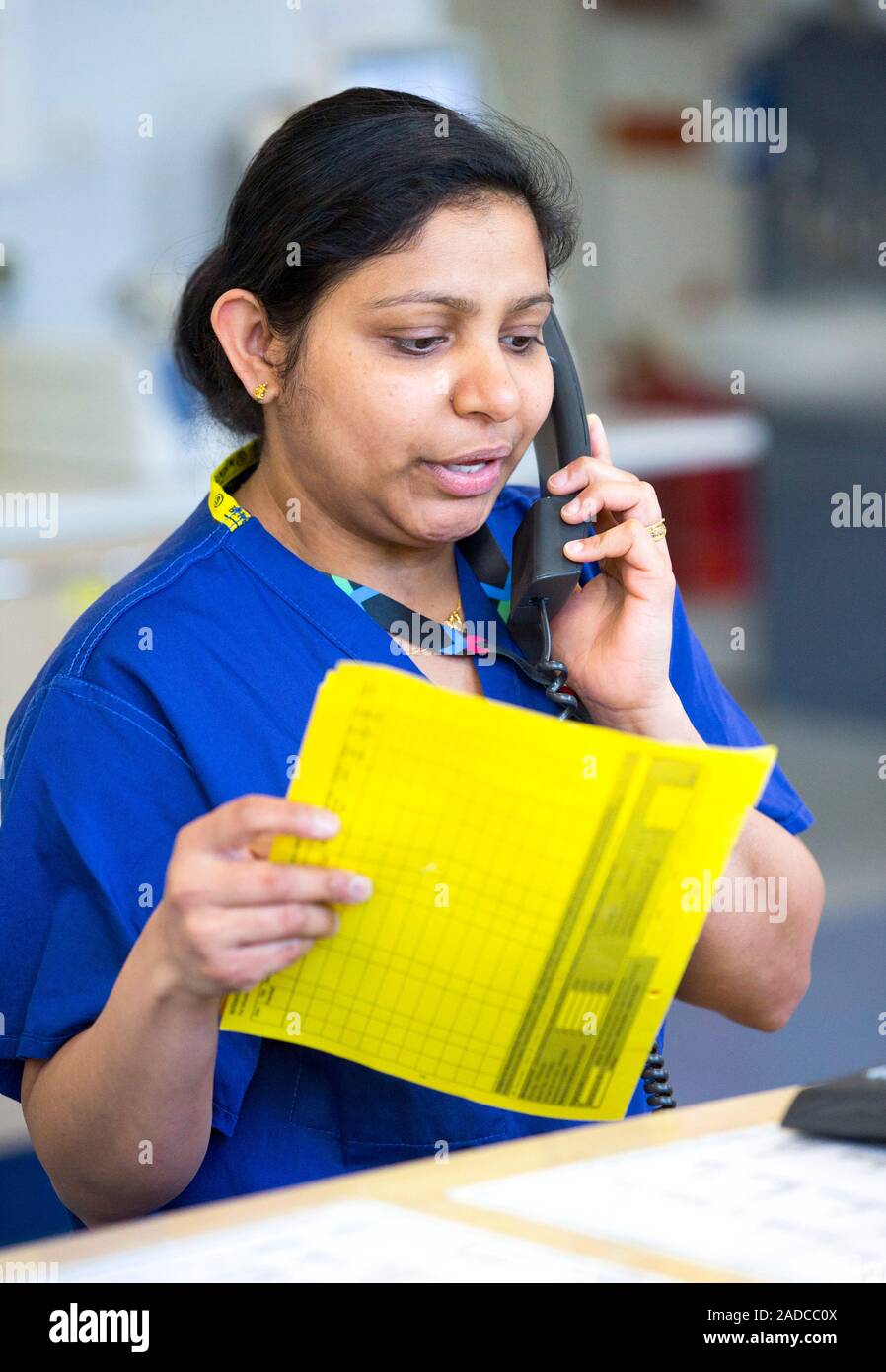 Hospital staff member using the telephone and handling patient notes ...