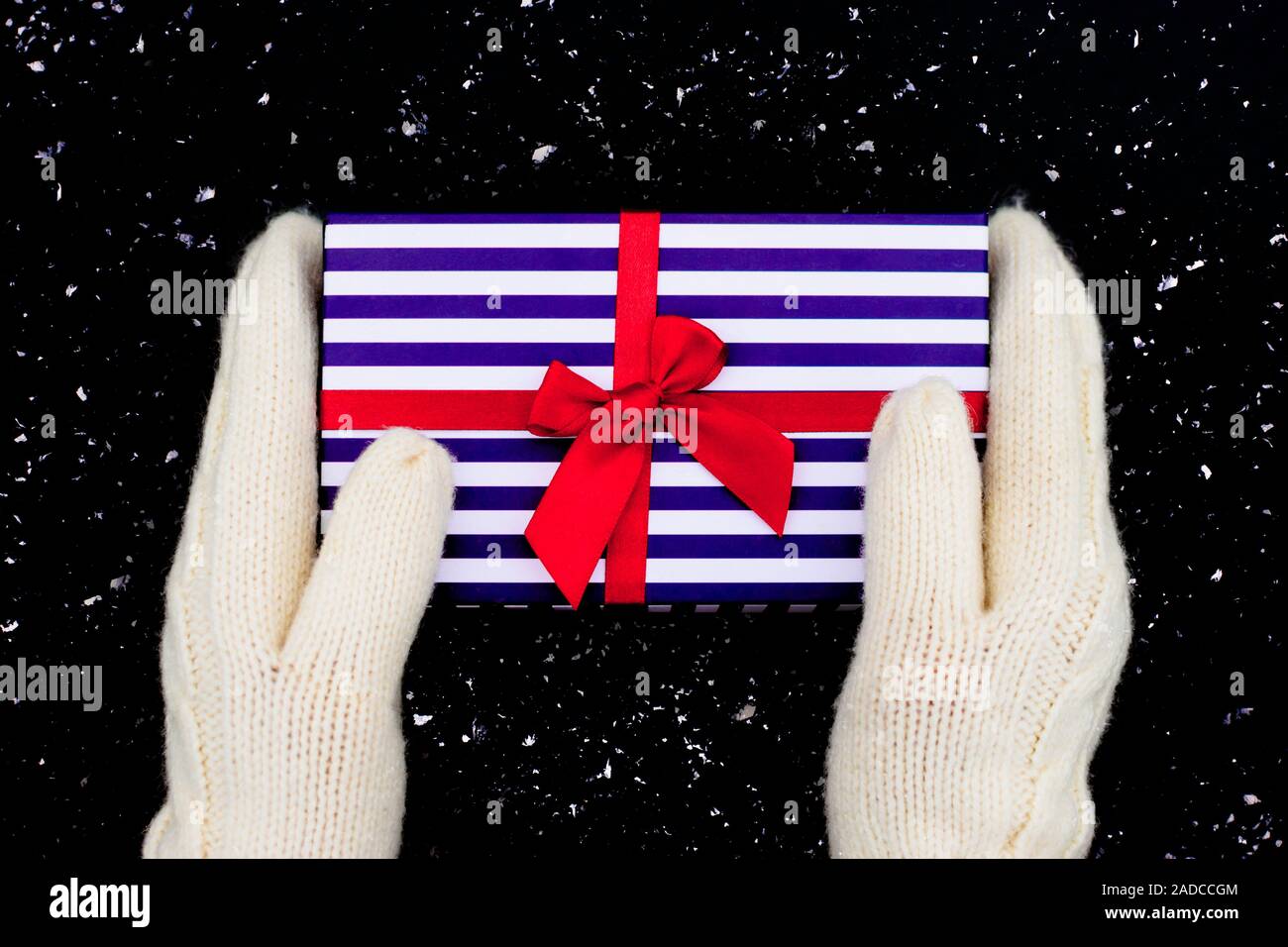 Hands in white winter mittens holding a gift striped box with a satin ...