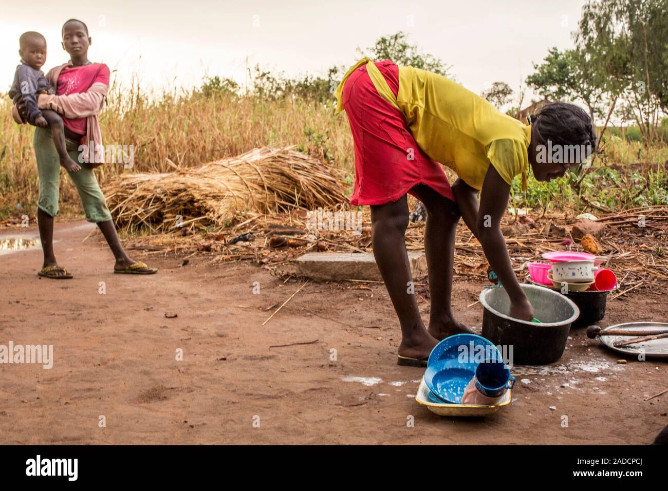 Mother washing dishes after a meal in a village, with her children at ...