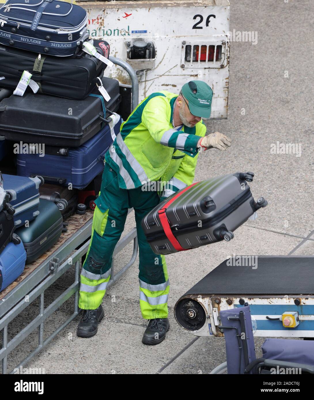 Man wearing yellow high-viz jacket loading bags from a trolley onto a ...
