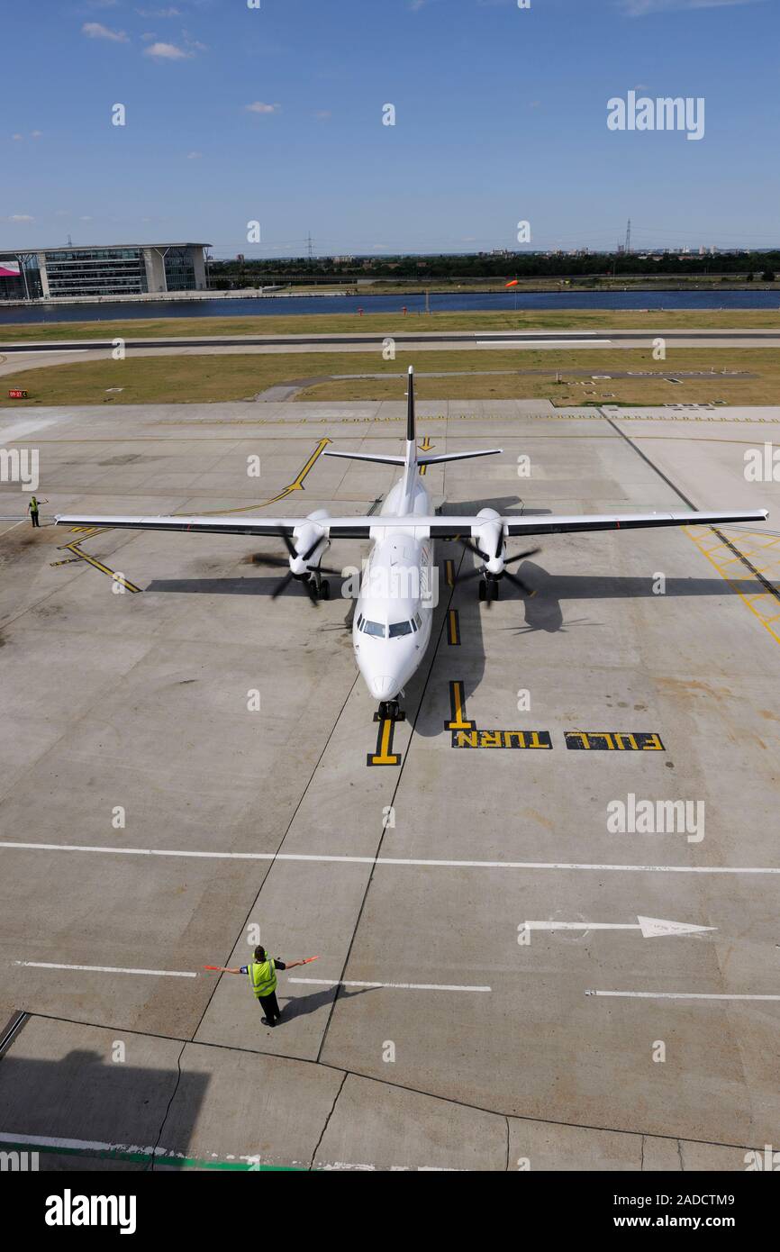 Marshaller with bats controlling Fokker F-50 taxiing at London City ...