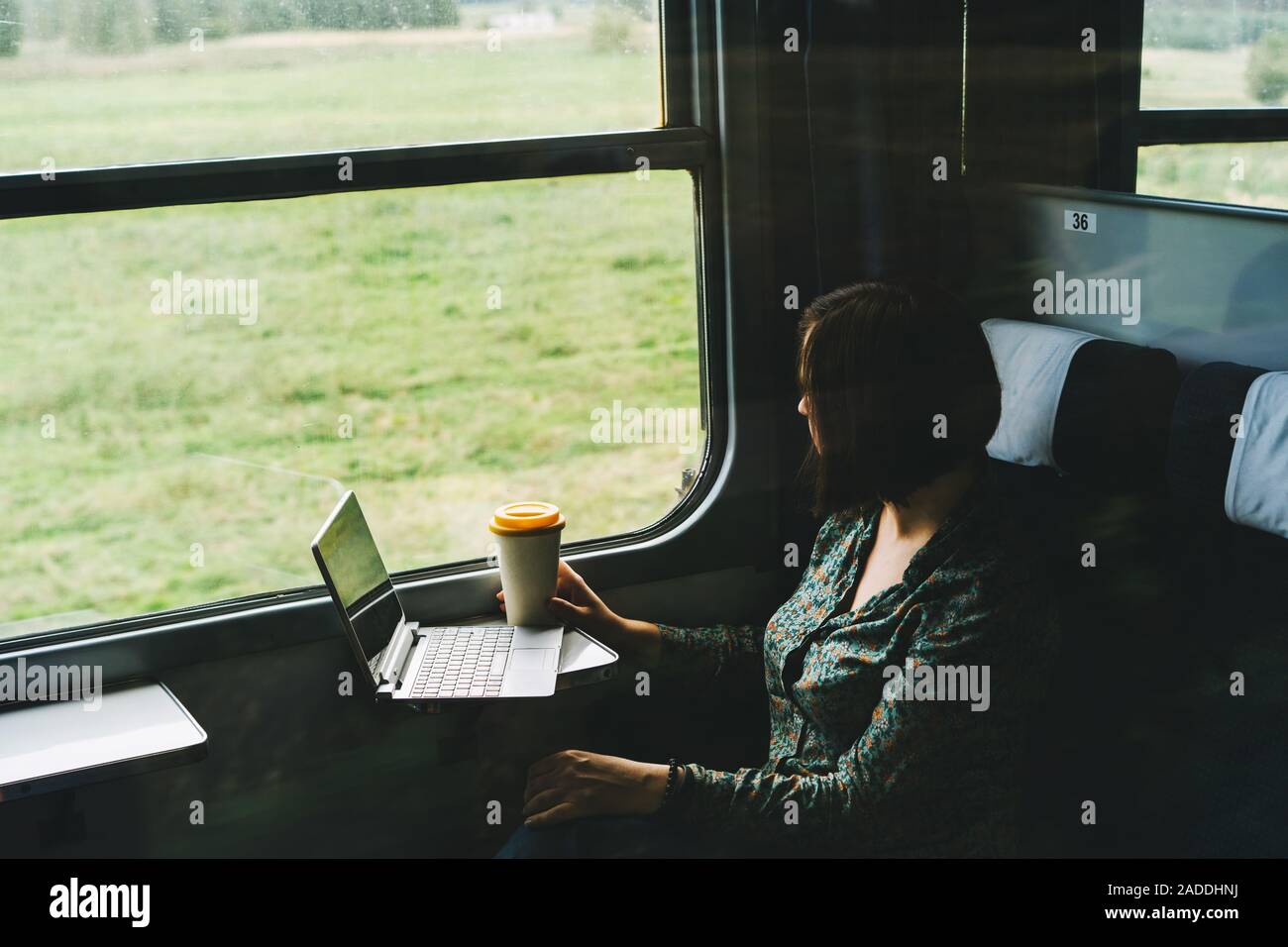 A woman sitting by the window of a commuter train with a laptop and ...