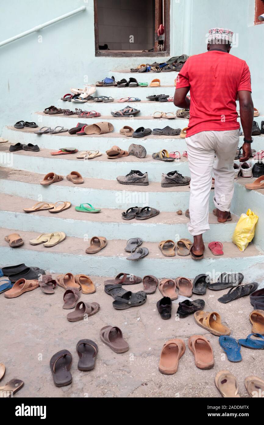 Man outside a mosque. Man taking his sandals off on steps arrayed with sandals and shoes left ...