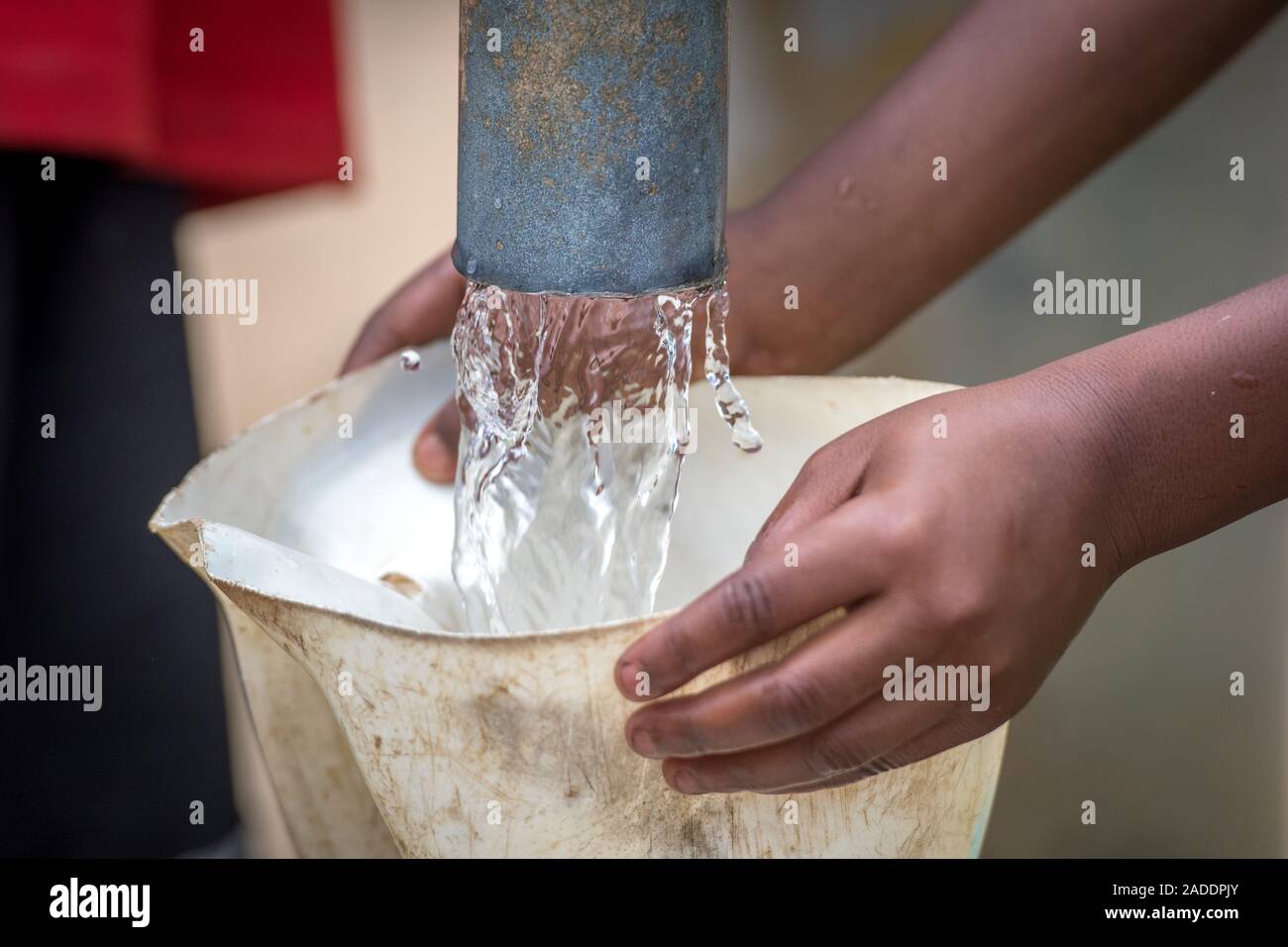 Small hands hold a funnel so that a water jug can be filled from a pump ...