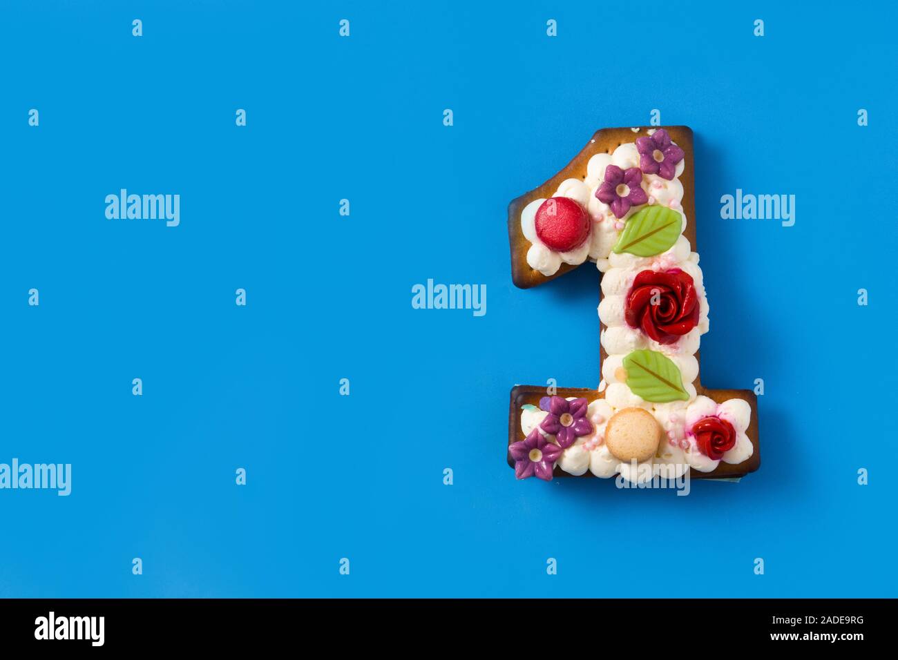Number one cake decorated with flowers, macarons on blue background ...