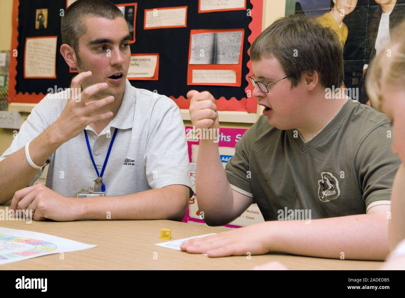 Boy with learning disability and teacher sitting at desk in classroom ...