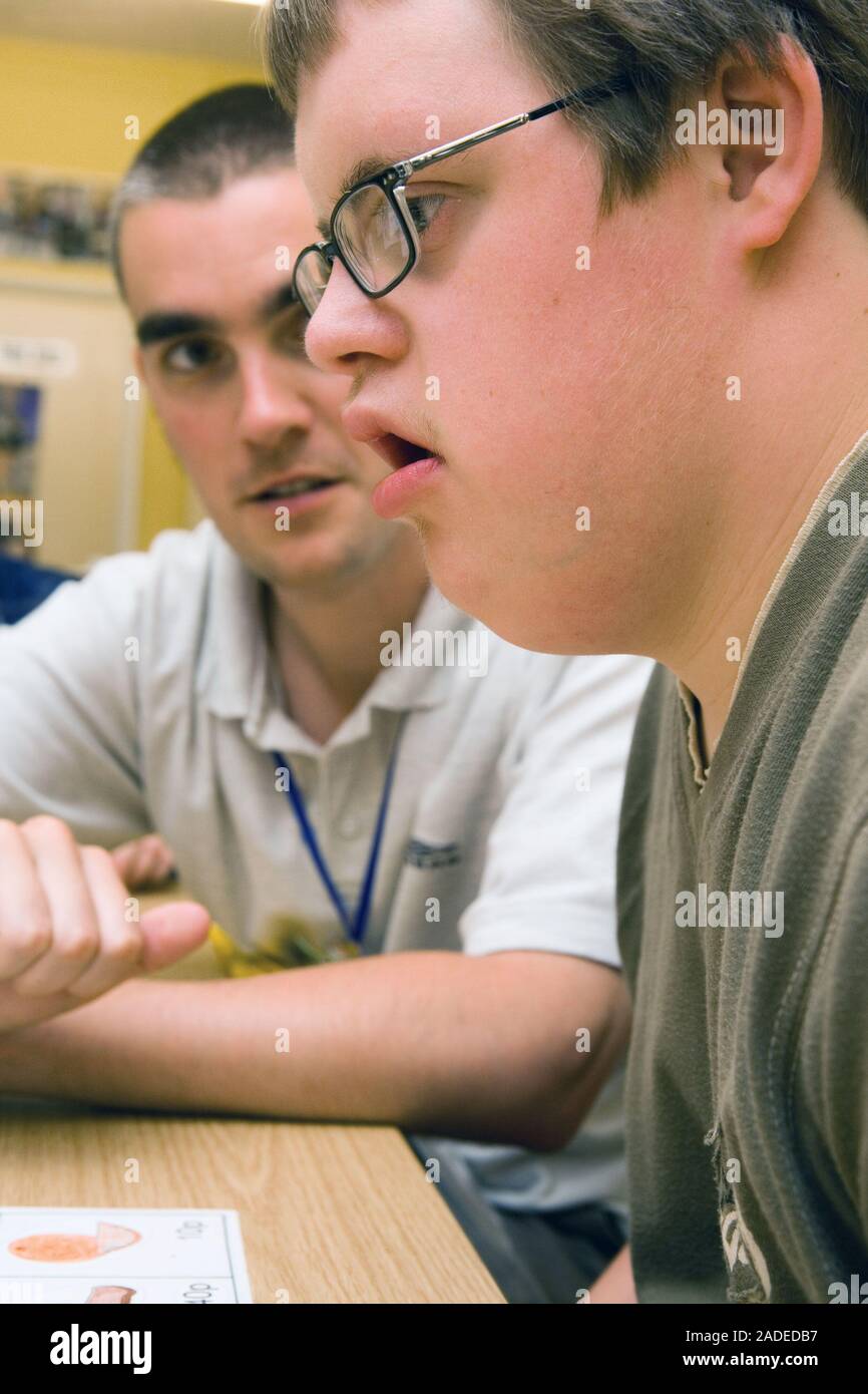 Boy with learning disability and teacher sitting at desk in classroom ...