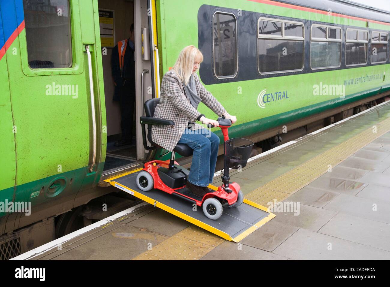 Woman steering electric mobility scooter down access ramp to board a ...