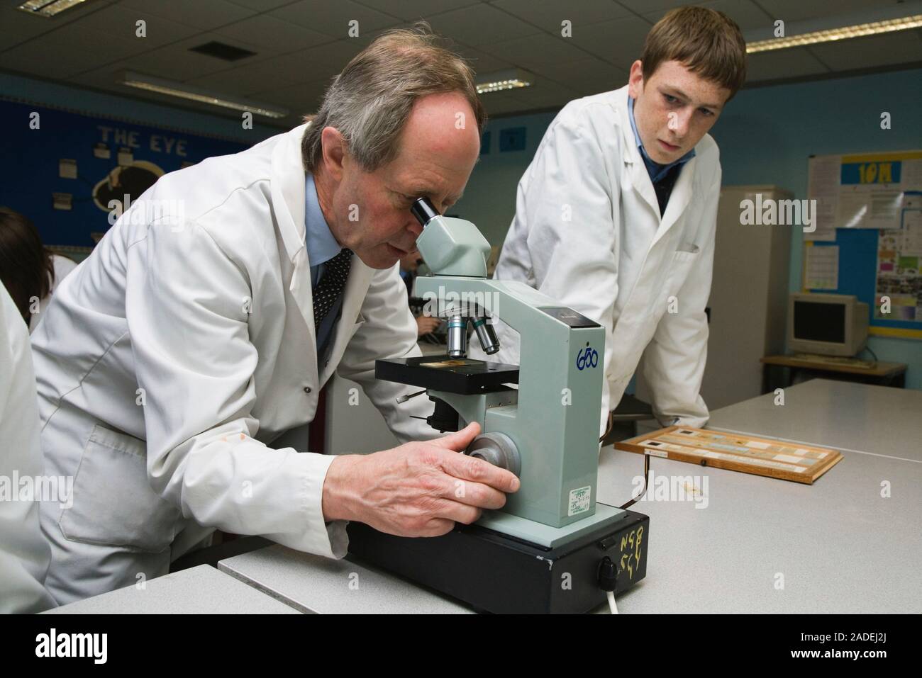 Secondary school teacher looking through a microscope in a science ...