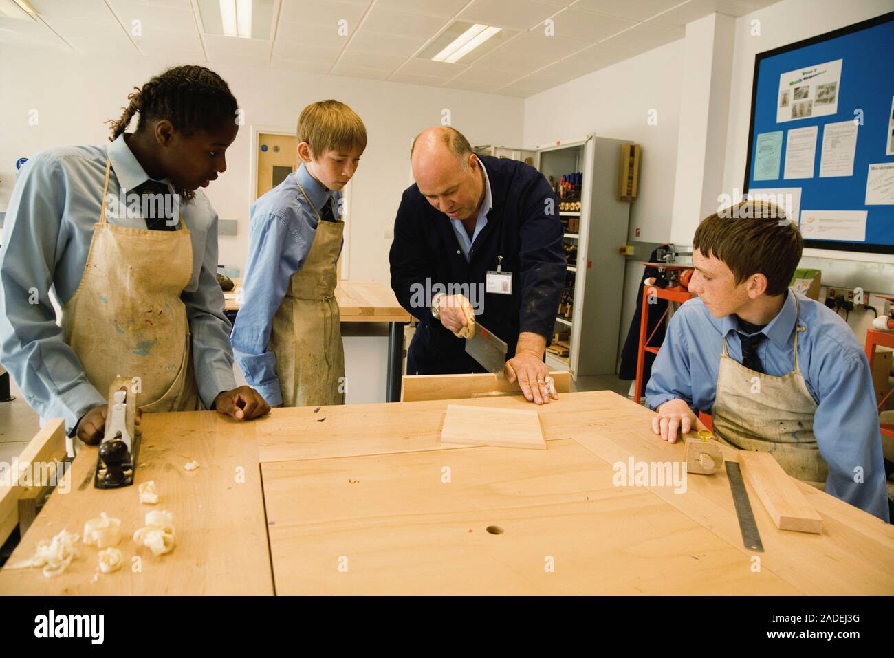 Woodwork teacher showing students how to saw wood in Design technology ...