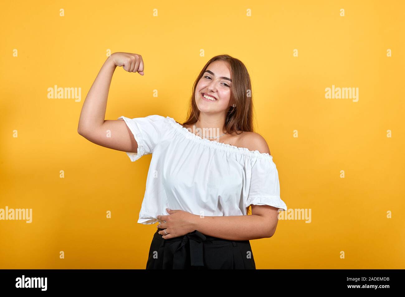 Strong charming young woman showing muscules, smiling on orange ...