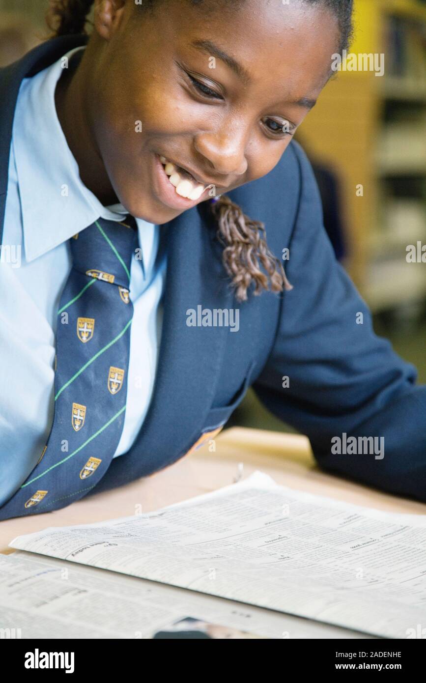 Secondary school student reading a newspaper in the school library ...