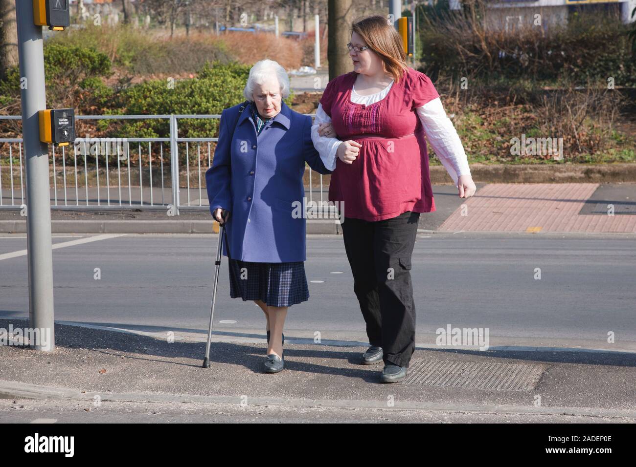 Carer helping elderly woman cross the road Stock Photo - Alamy