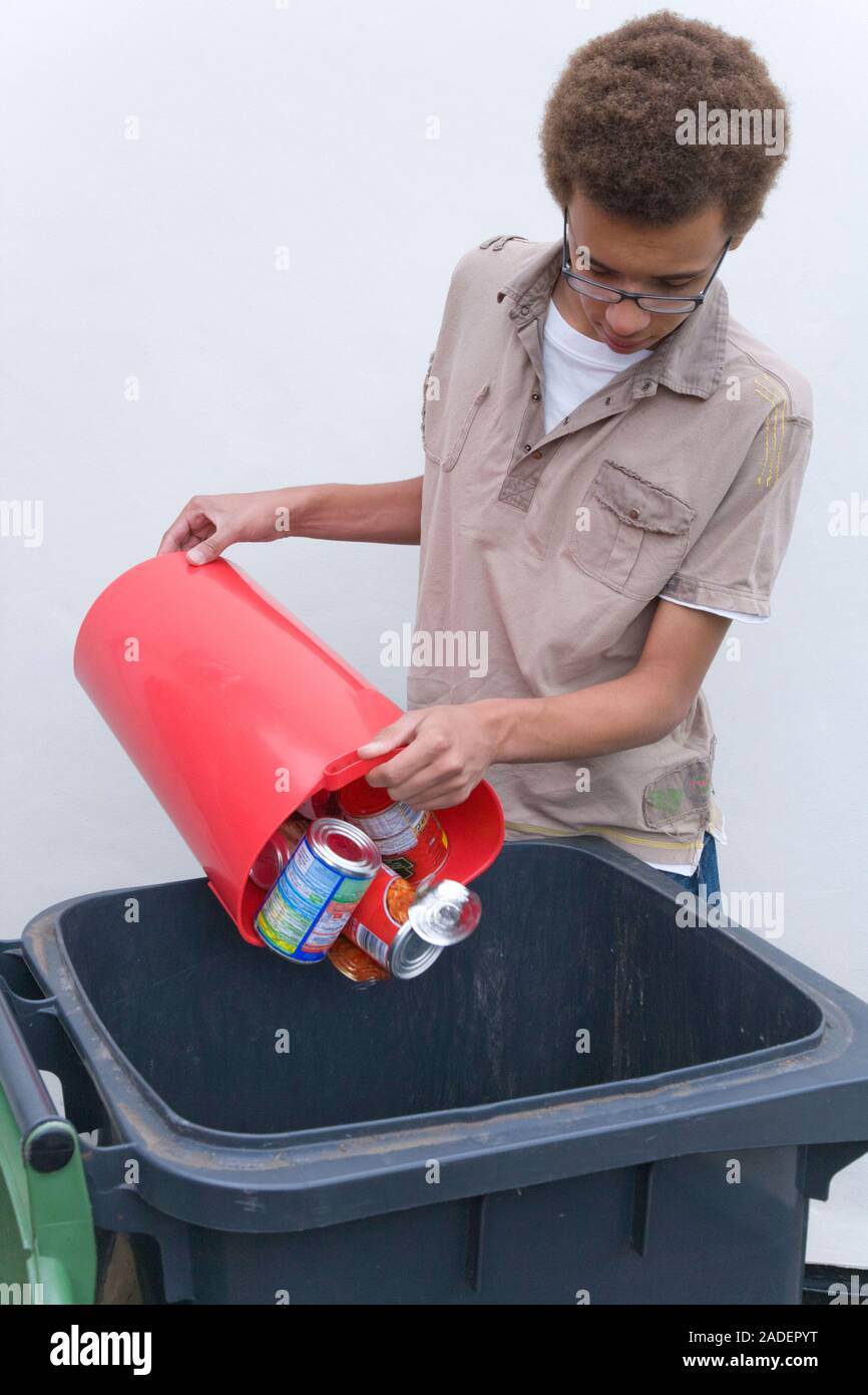 Teenage boy putting tins and cans into recycling wheelie bin ready for ...
