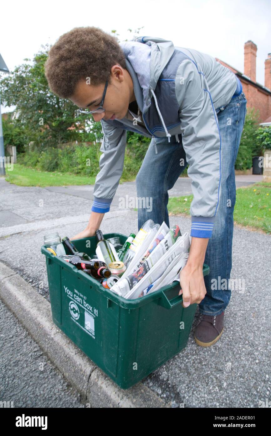 Teenage boy placing curb side recycling collection box on the pavement ...