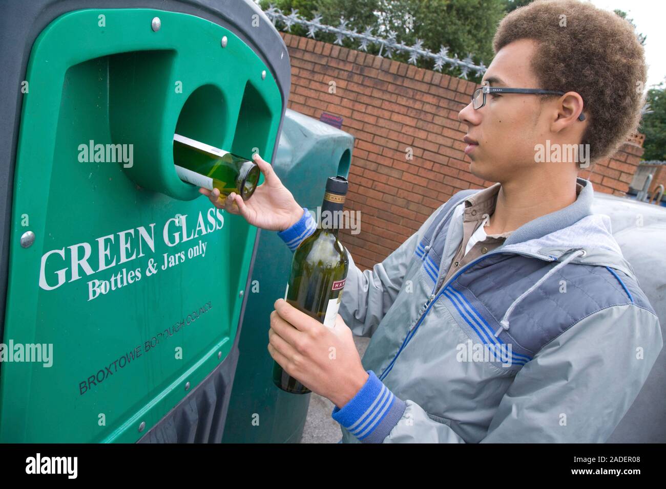 Teenage boy putting bottles in a green glass and jars into a recycling ...