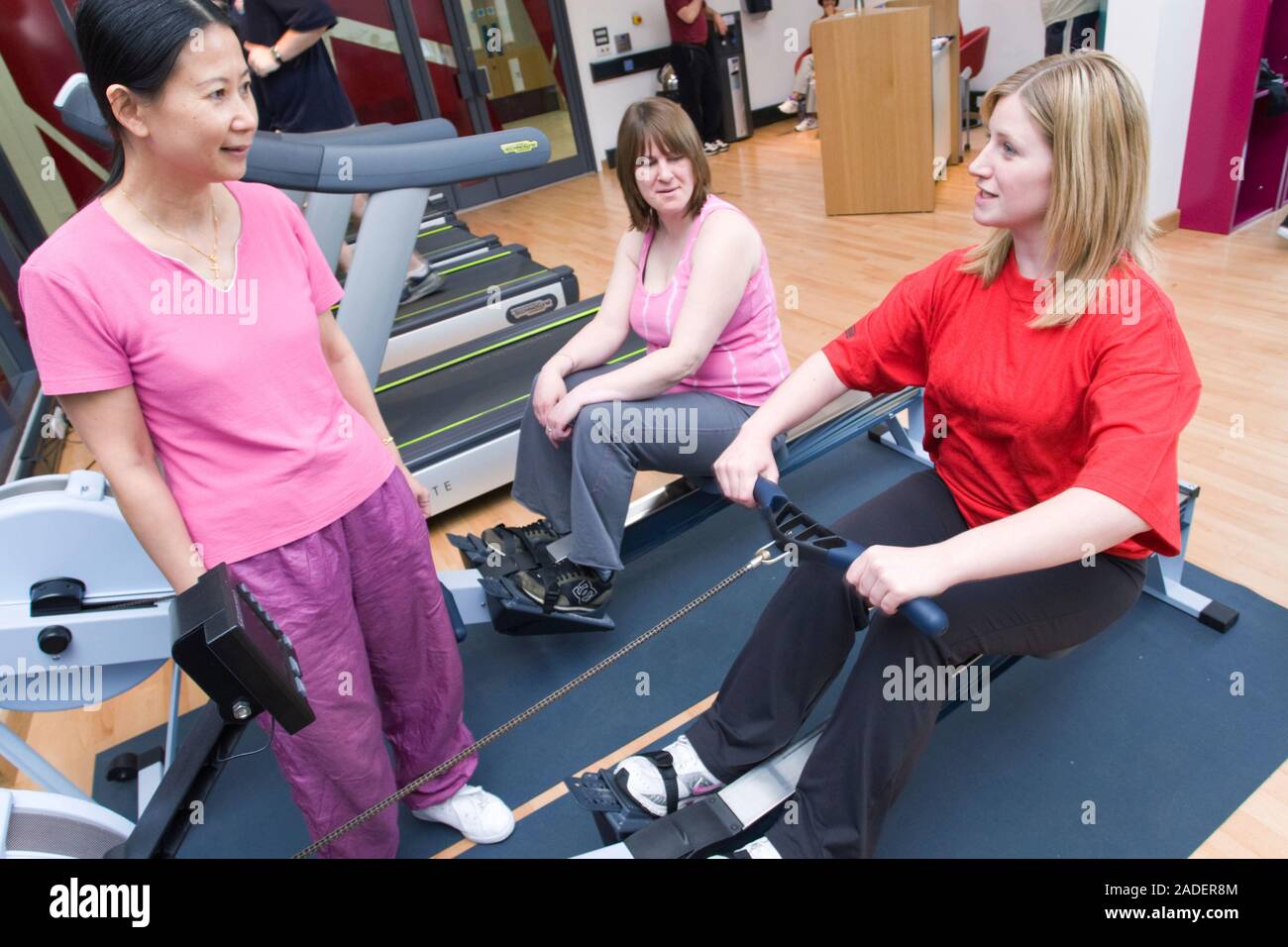 Fitness instructor showing two women how to use the rowing machine at ...