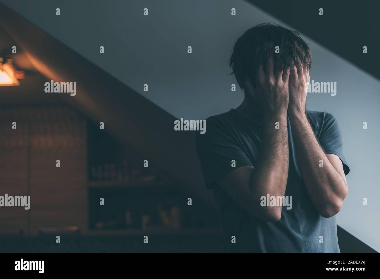 Depressed man is crying by the window of kitchen loft, hands covering ...