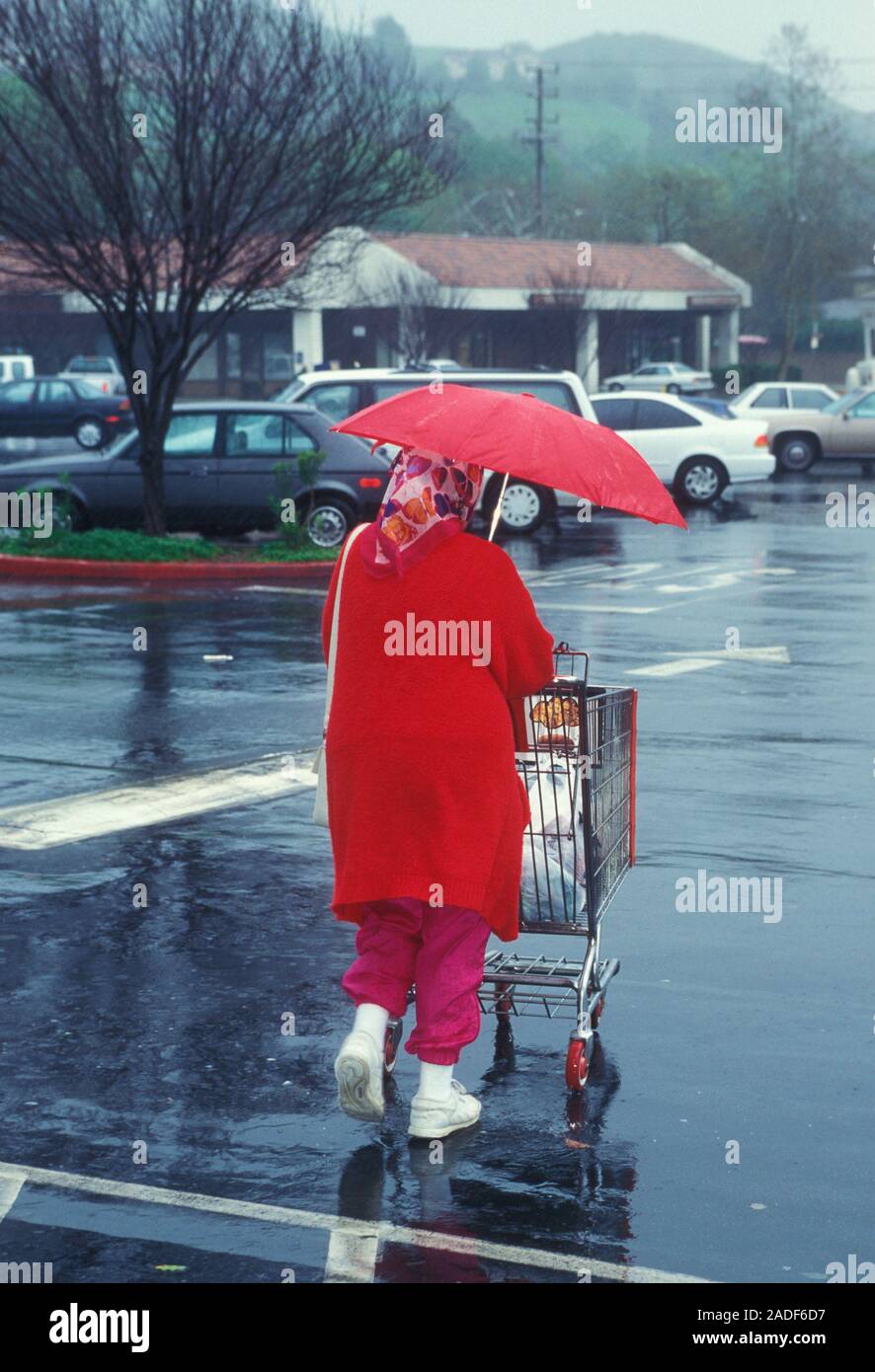 Woman shopping in the rain. Woman pushing a supermarket trolley through ...