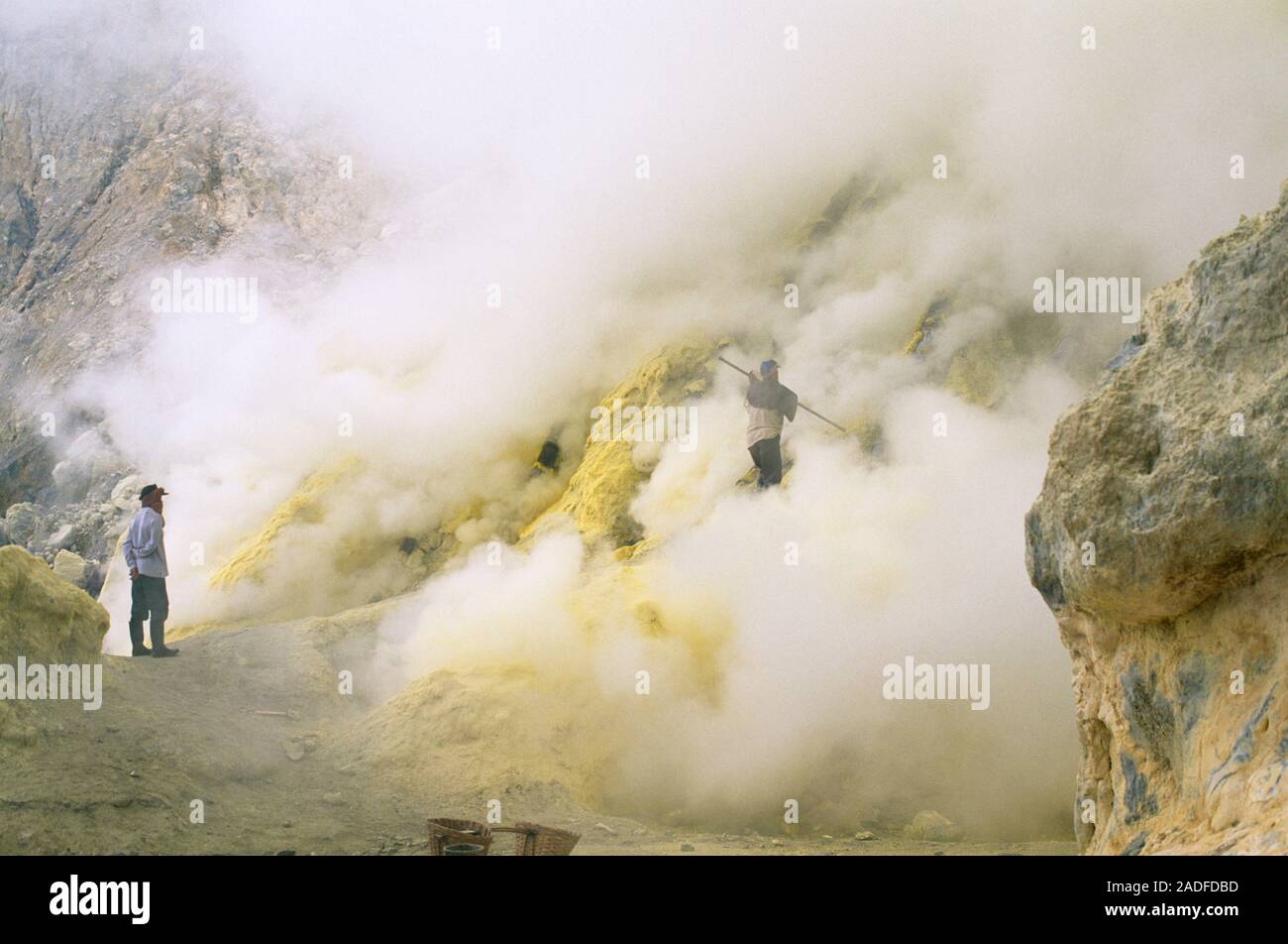 Volcanic sulphur mining. Men mining solid sulphur (yellow) on the Kawah ...