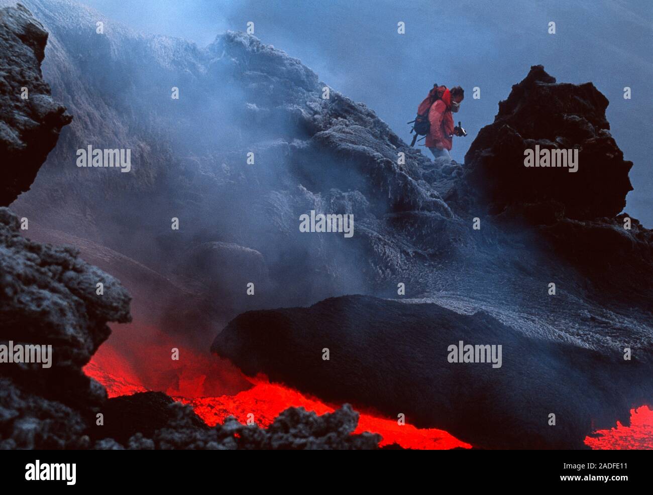 Volcanologist wearing a gas mask and holding a camcorder as he stands ...