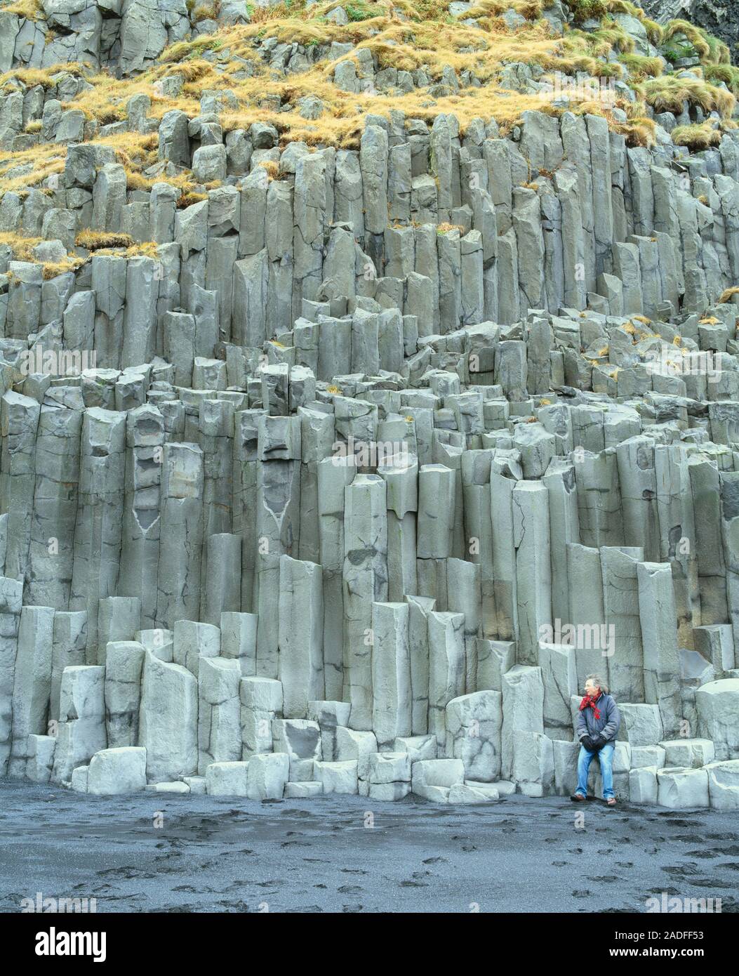 Basalt columns. Tourist sitting on columns of basalt by a black sand ...
