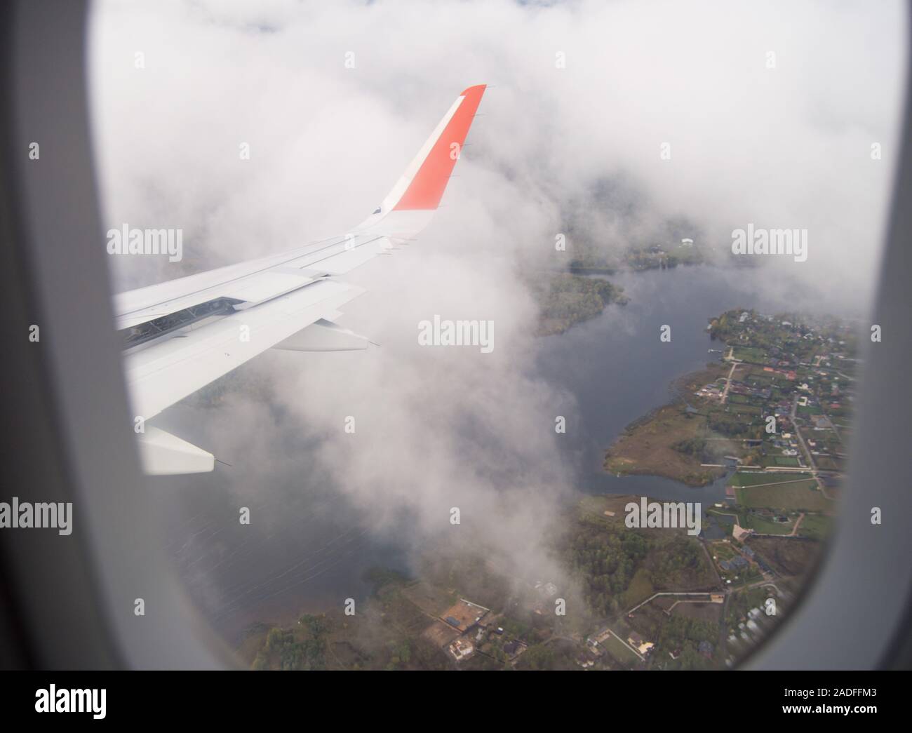 A bird's eye view of the wing in the clouds and the ground with houses ...