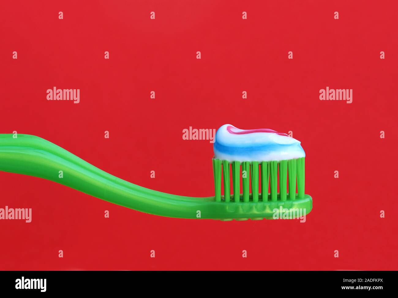 green toothbrush with striped toothpaste in front of a red background ...