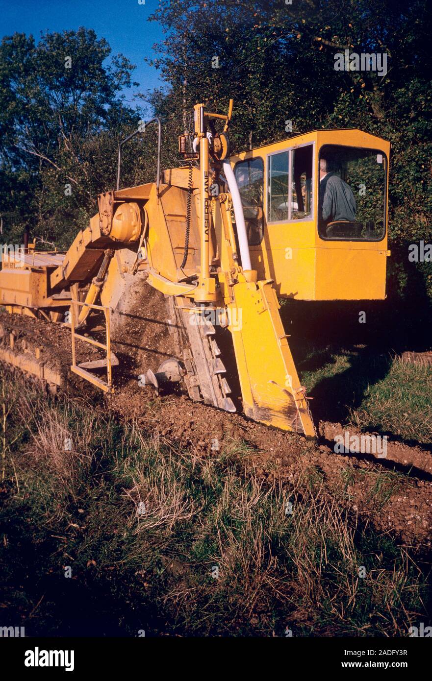 Machine digging a trench and laying drainage pipe Stock Photo - Alamy
