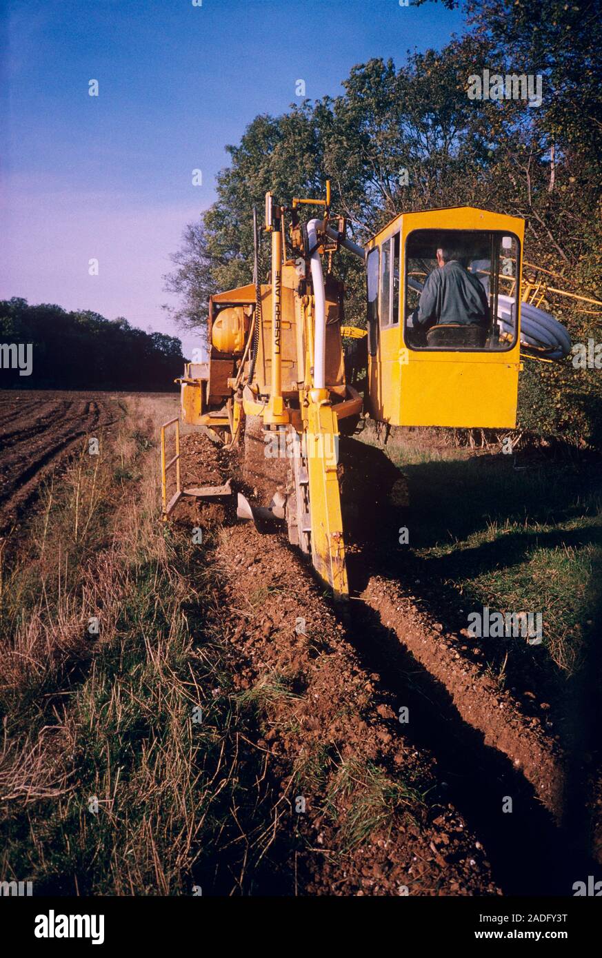 Machine digging a trench and laying drainage pipe Stock Photo - Alamy