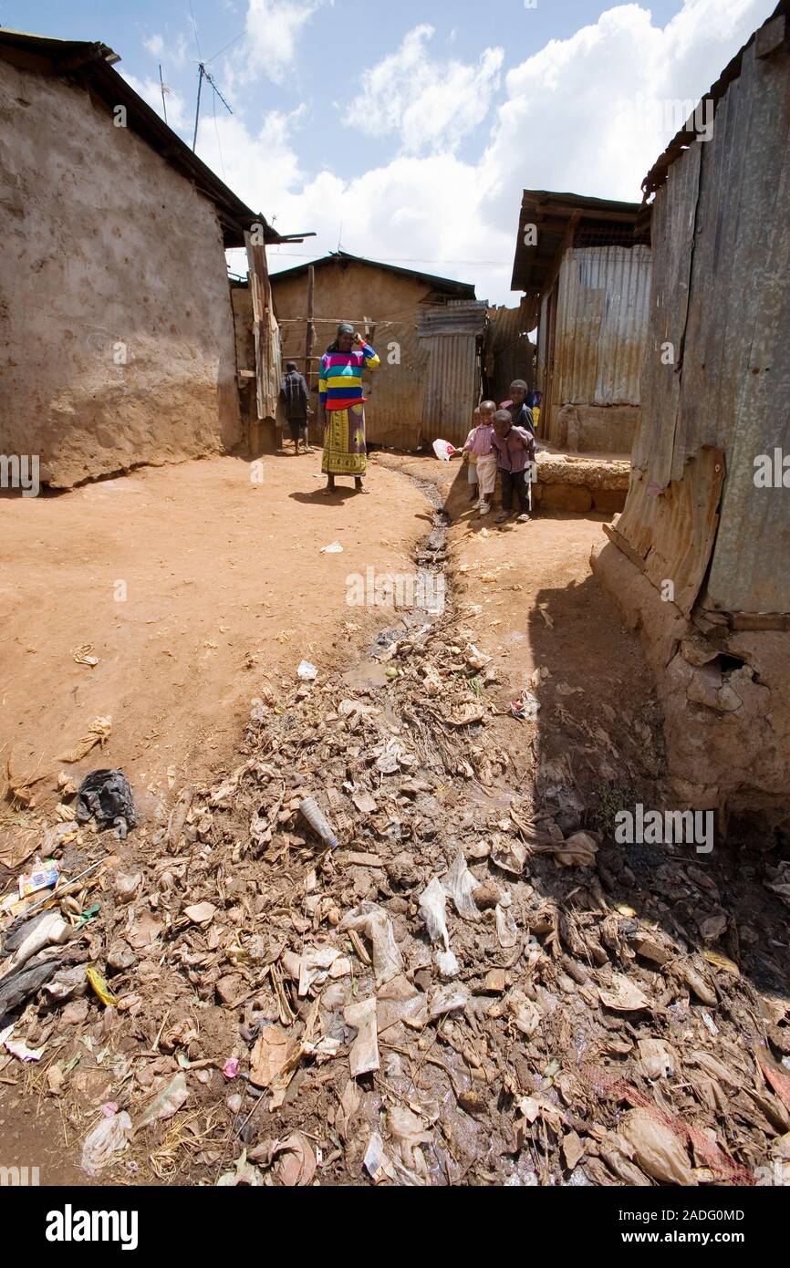 Slum housing. Family standing by a waste drainage ditch in a slum. Lack ...