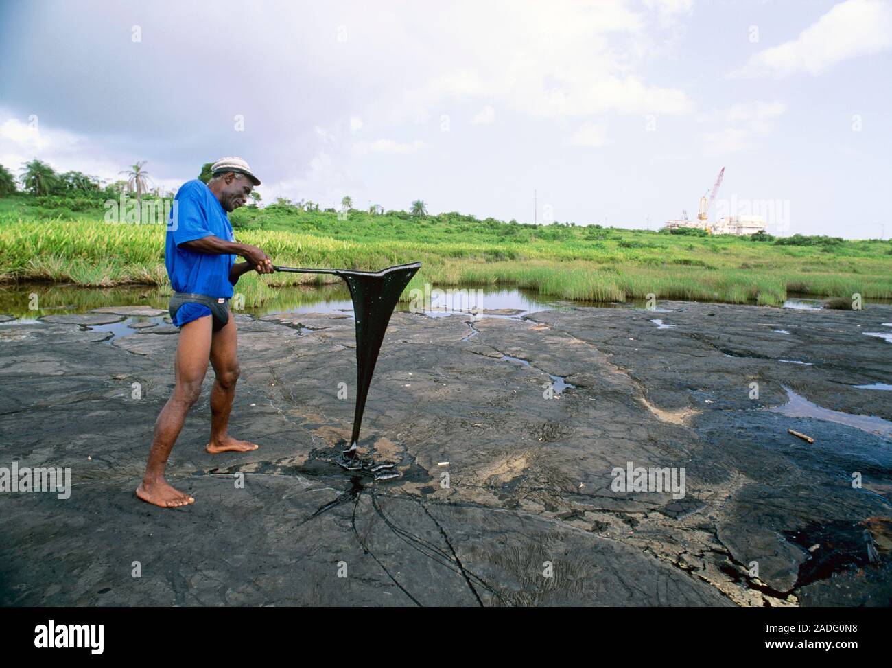 Asphalt lake. Worker holding a stick coated in melting asphalt ...