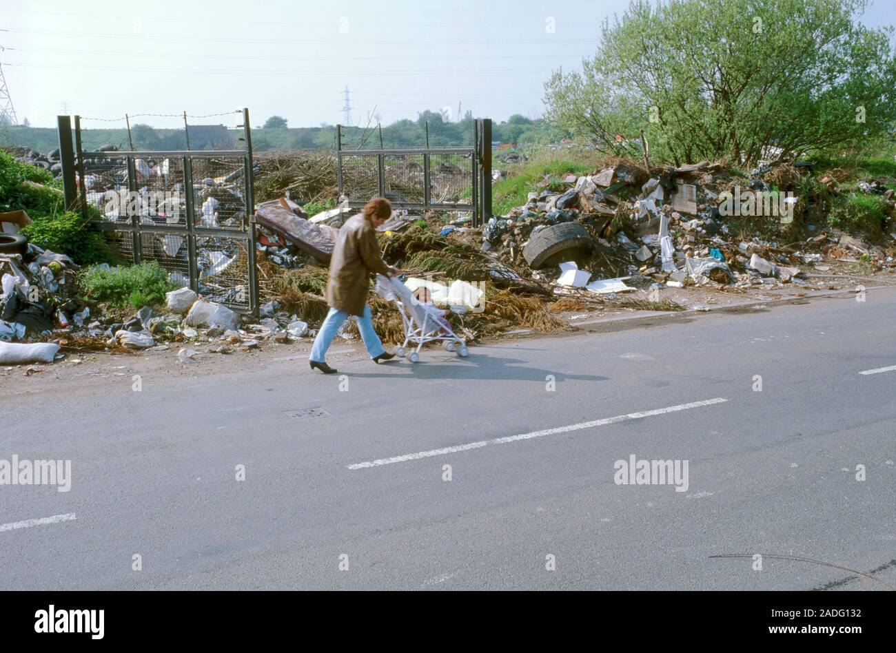 Fly-tipping. Woman pushes a pram past a pile of fly-tipped rubbish. Fly ...
