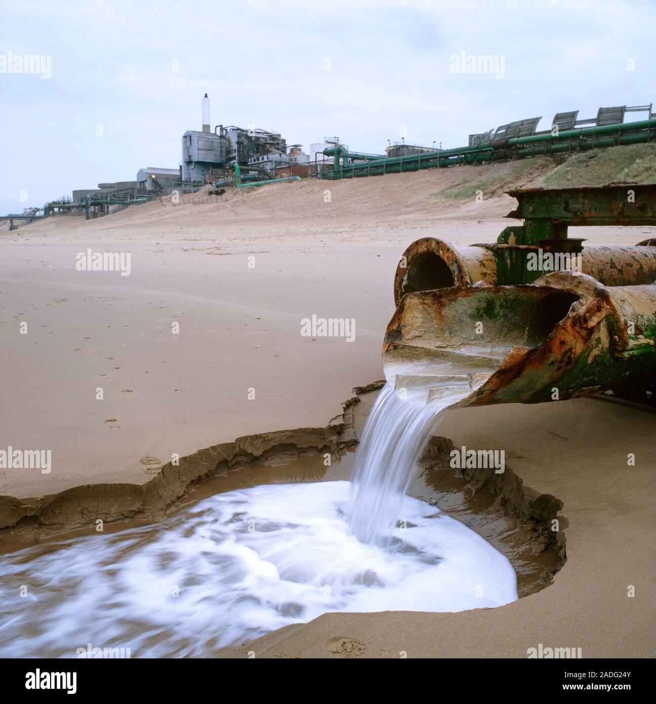 Industrial pollution. Outflow pipe discharging wastewater onto a beach ...