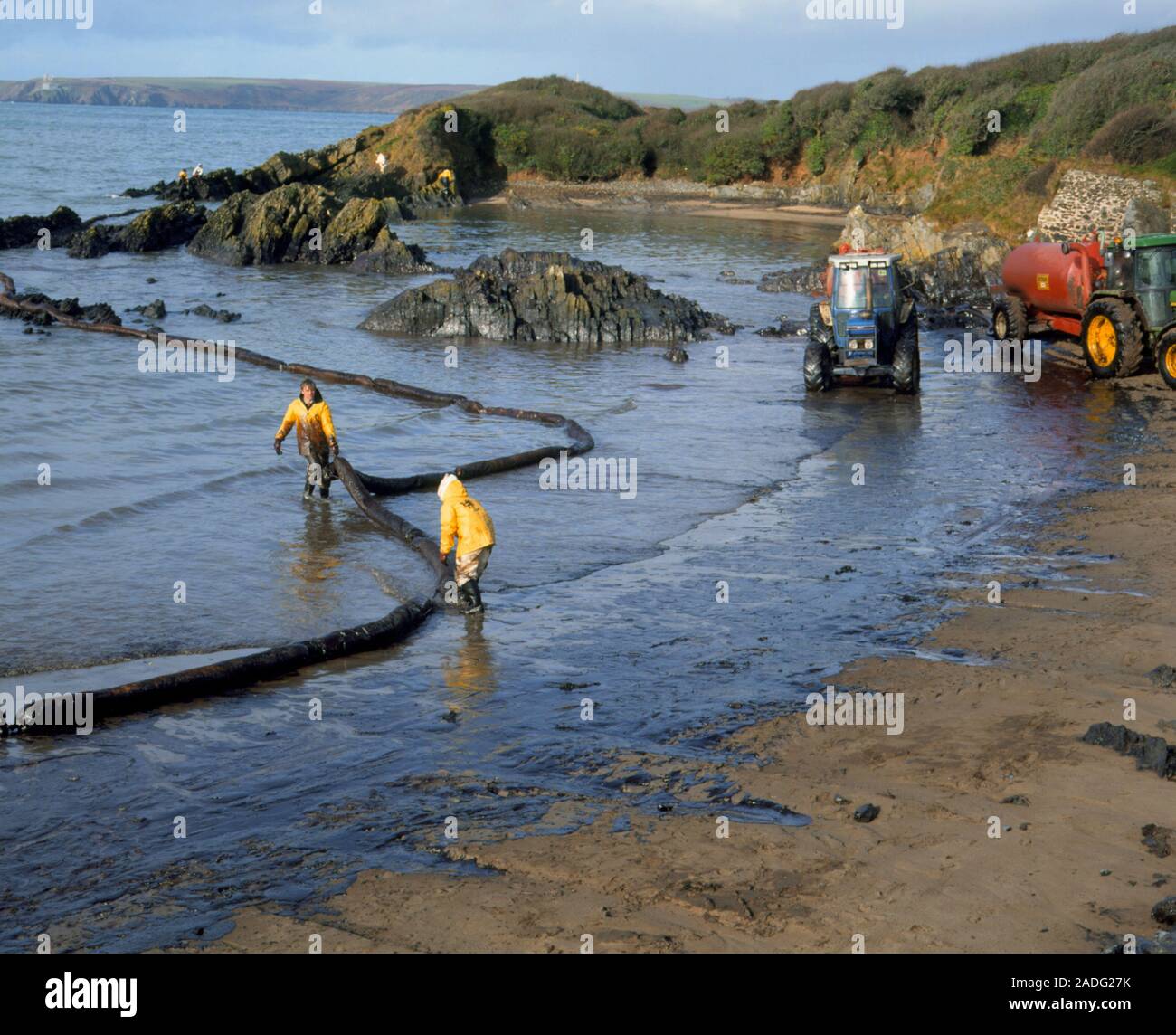 Oil pollution clean-up. Team of workers cleaning up a beach polluted by ...