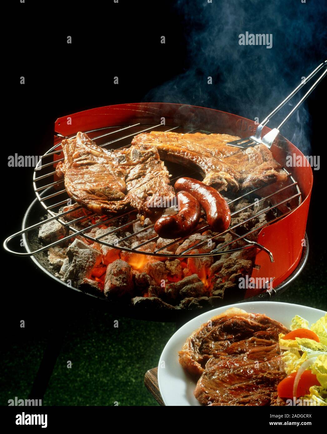 Barbecue. Chops and sausages cooking over a free- standing metal ...