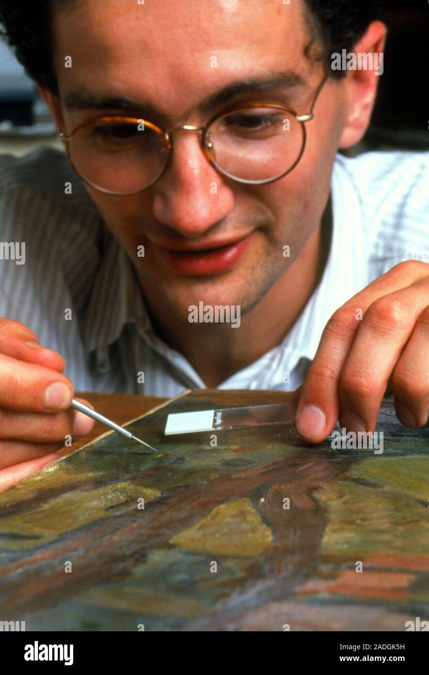 Art forgery detection. Technician uses a needle to remove a tiny paint ...