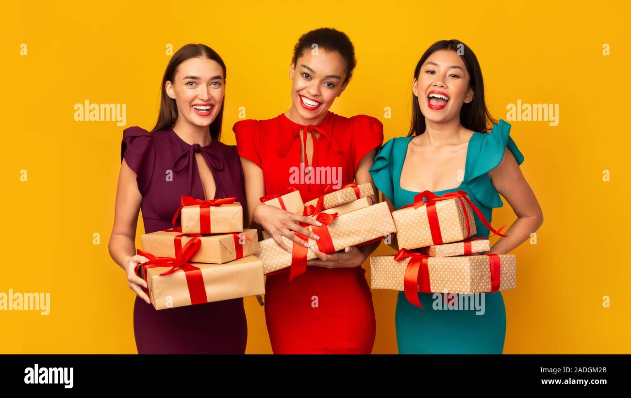 Three Models In Dresses Holding Wrapped Boxes Over Yellow Background ...