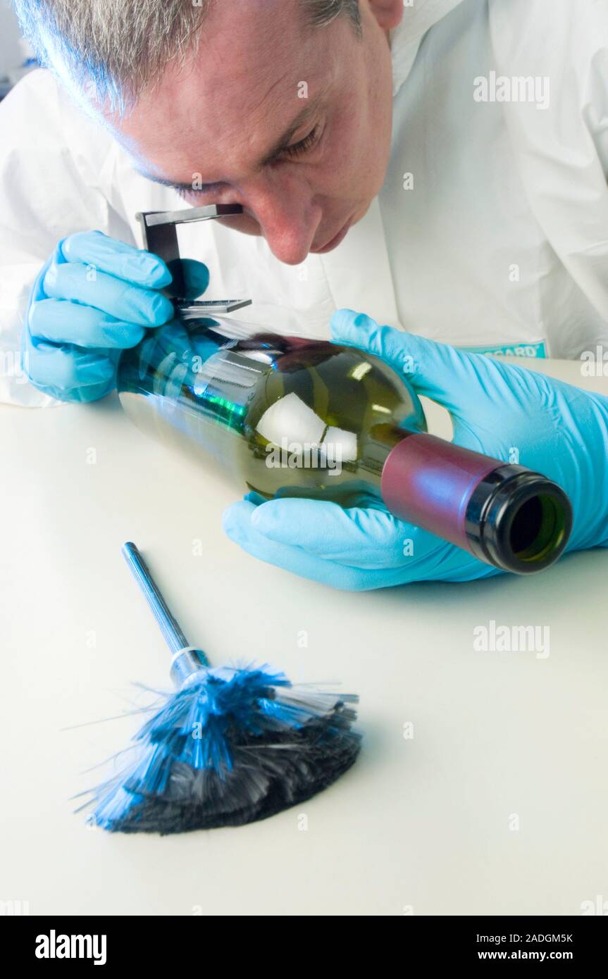 Forensic evidence. Forensics officer examining a wine bottle with a ...