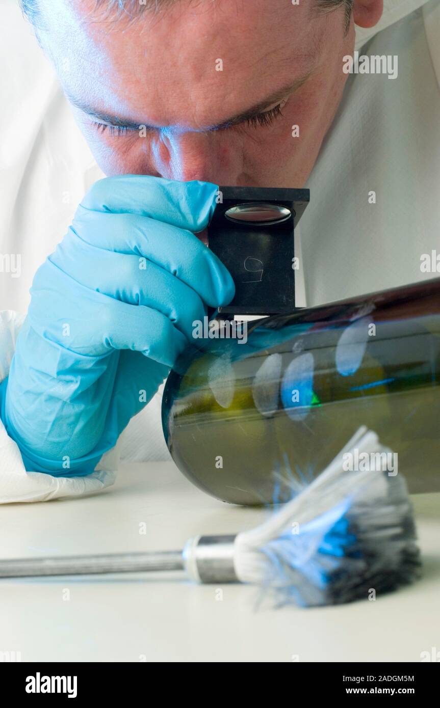Forensic evidence. Forensics officer examining a wine bottle with a ...